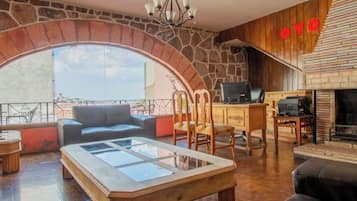 Uma sala de estar aconchegante com arco de pedra, lareira e grande janela com vista para a cidade.