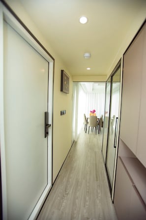 Corredor de hotel com piso de madeira, área de refeições com mesa e cadeiras e uma porta à esquerda.