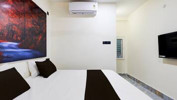 Quarto de hotel com cama, televisão montada, ar condicionado e um quadro grande na parede.