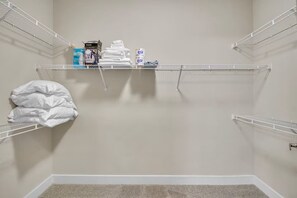 Armário com prateleiras aramadas, pilha de toalhas dobradas e caixa de detergente para roupa.