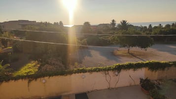 Área residencial com rua pavimentada, vegetação e um edifício com telhado plano.