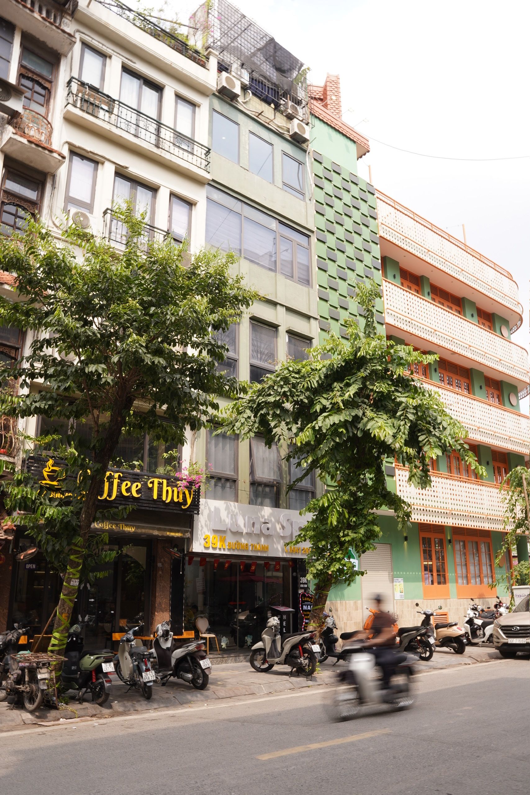 Vista da rua com uma cafeteria chamada 'Coffee Thuy' e vários scooters estacionados.