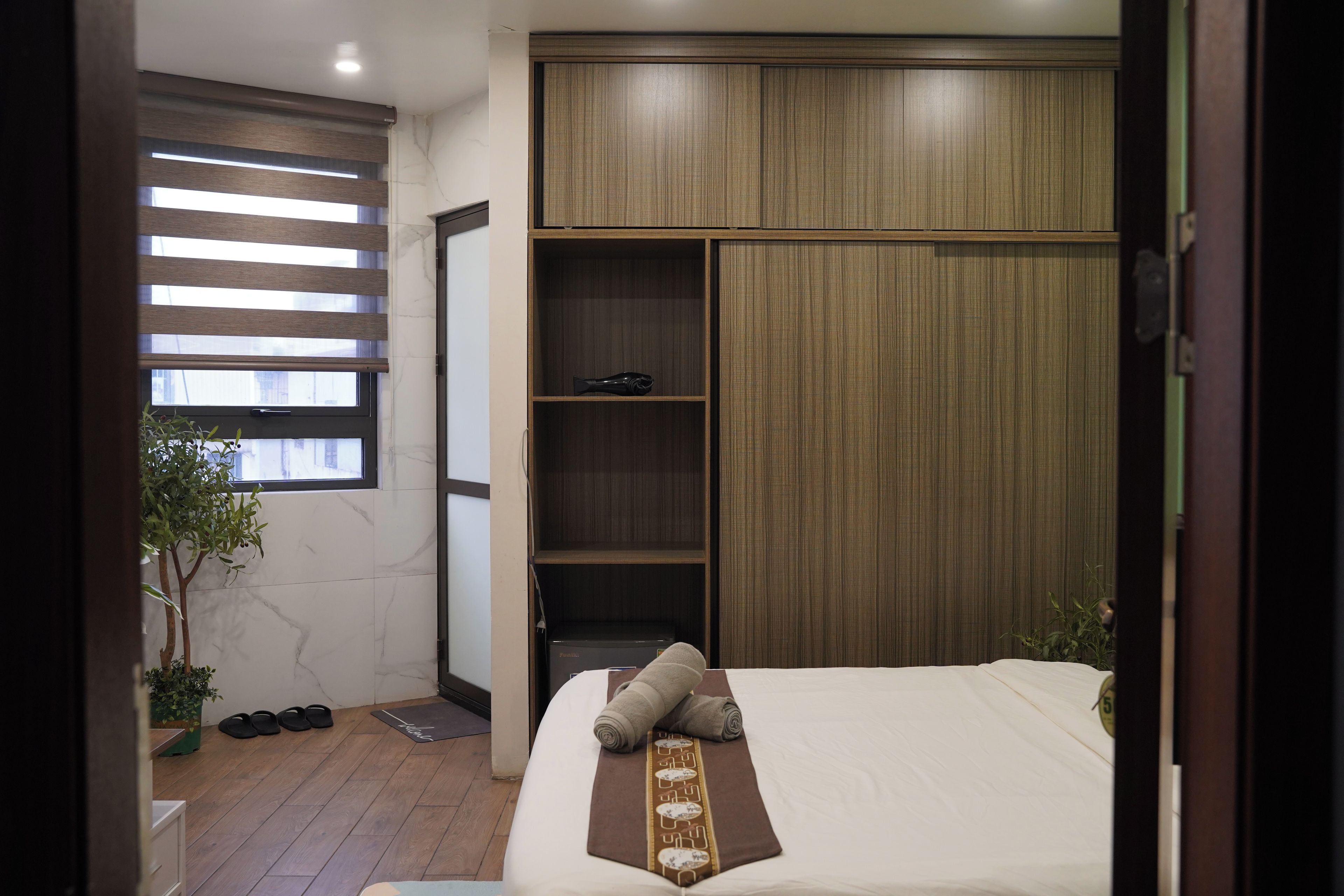 Quarto com cama, guarda-roupa, estante, janela e planta em vaso.