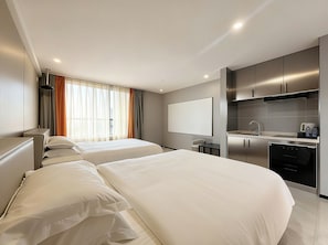 Quarto de hotel com duas camas, uma cozinha compacta e uma janela grande com cortinas.