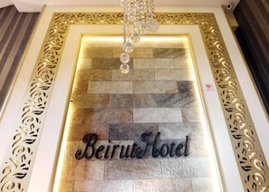 Um letreiro com o texto 'Beirut Hotel' em fonte decorativa, cercado por padrões dourados ornamentados.