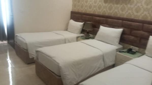 Quarto de hotel com duas camas, uma mesa de cabeceira com abajur e parede estampada.