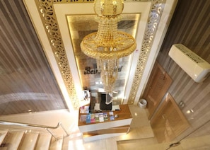 Uma área de recepção com um candelabro, um balcão com folhetos e uma escadaria.