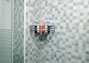 Canto de um banheiro com parede revestida de azulejos e uma prateleira de metal com artigos de higiene pessoal.