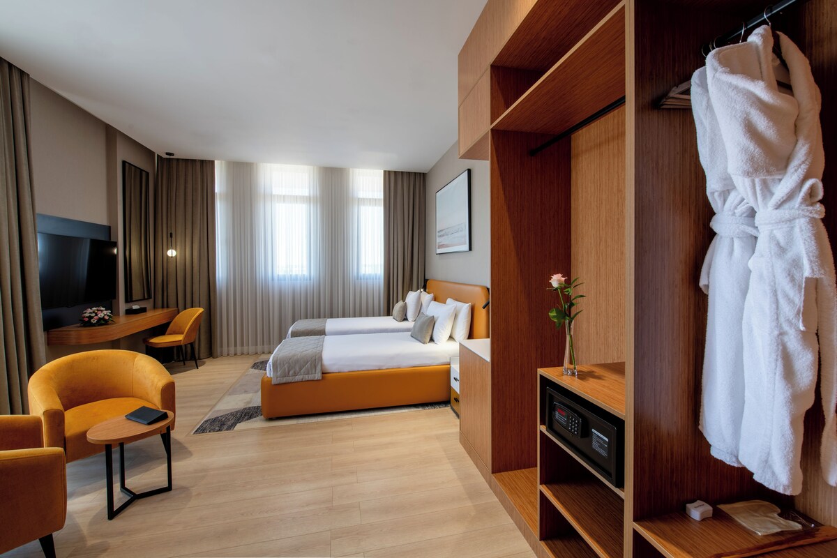 Quarto de hotel com cama, escrivaninha, cadeira, televisão e roupão pendurado em um suporte.