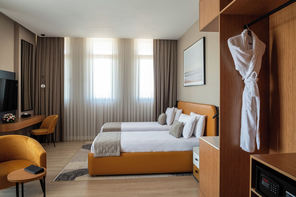 Quarto de hotel com cama, escrivaninha, cadeira e televisão.