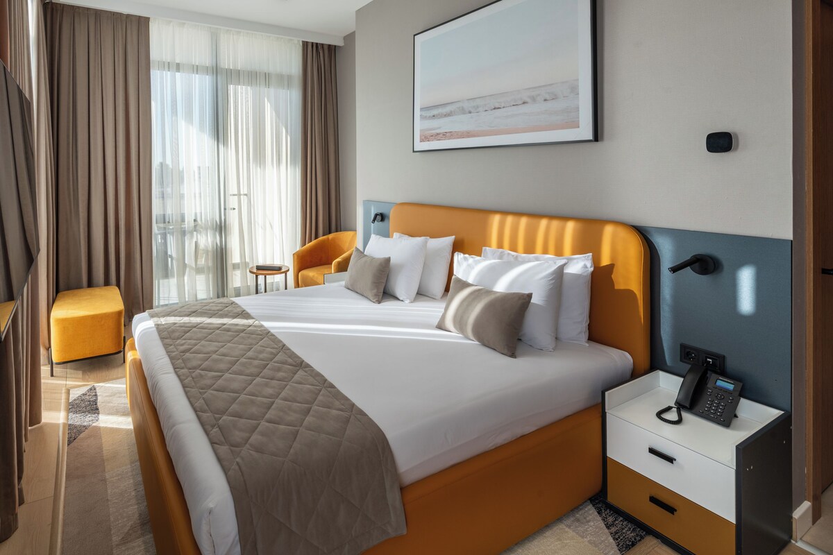 Quarto de hotel com cama, mesa de cabeceira, cadeira e um quadro na parede.