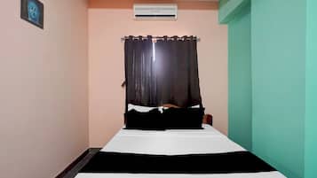 Um quarto pequeno com uma cama, cortina, ar condicionado e porta.