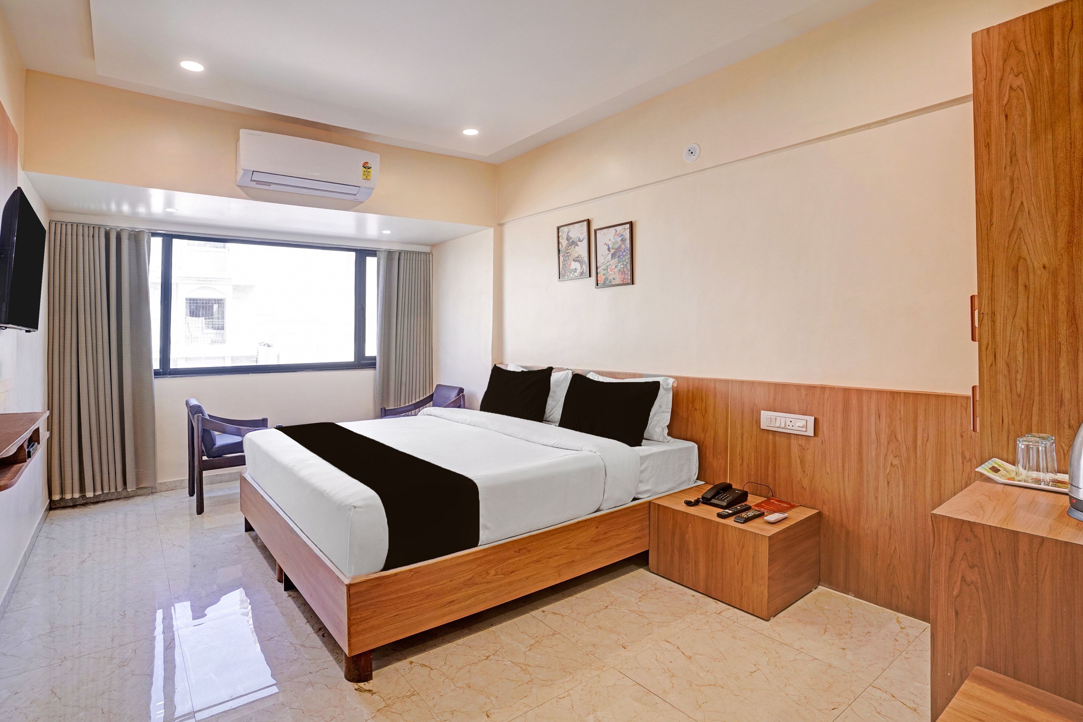 Quarto de hotel com cama, escrivaninha, cadeira, janela com cortinas e ar condicionado fixado na parede.