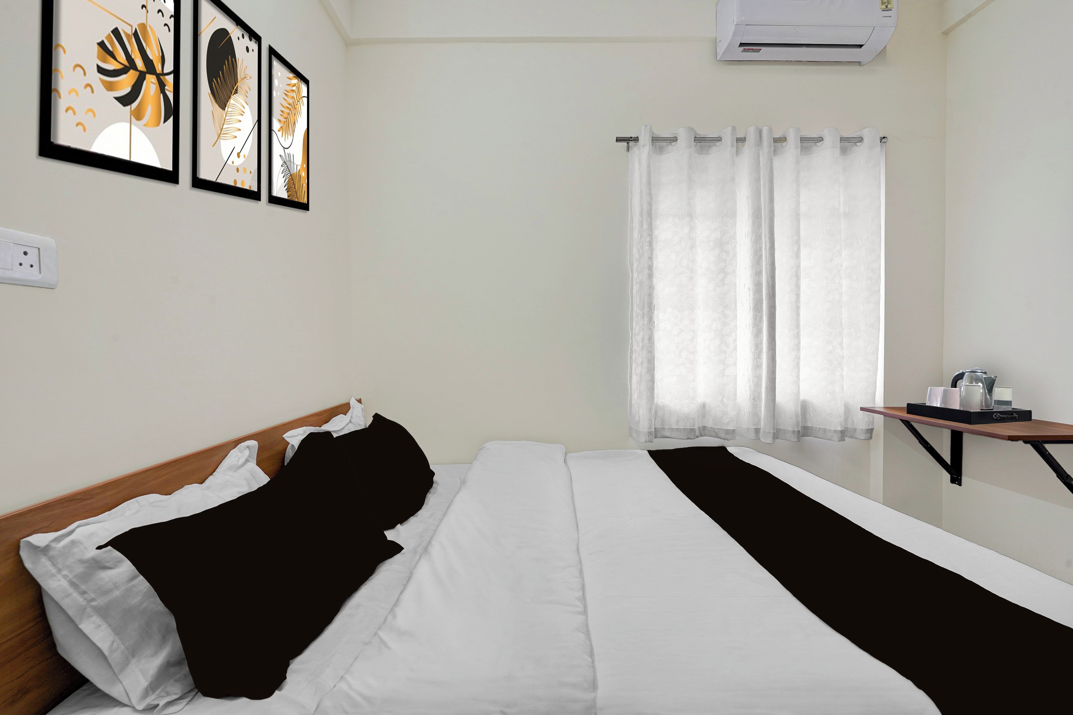 Quarto de hotel com cama, mesa de cabeceira com chaleira e duas obras de arte emolduradas na parede.