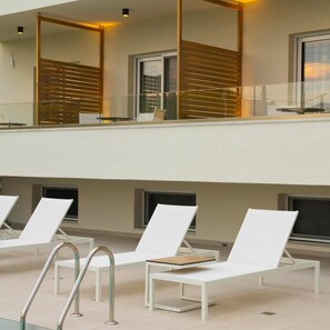 Uma área de estar ao ar livre moderna, com poltronas confortáveis brancas e piscina.