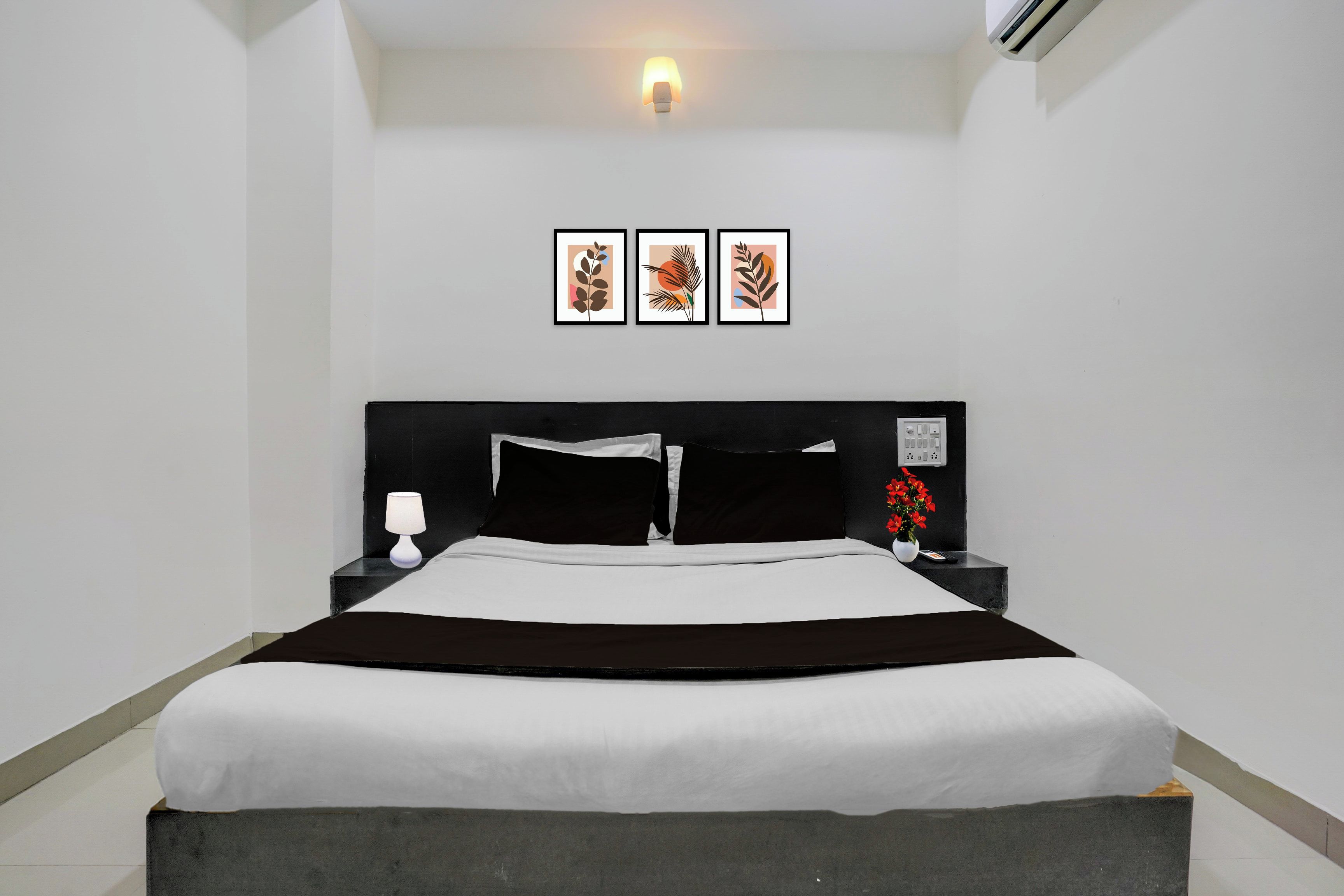 Cama bem arrumada com esquema de cores preto e branco, mesa de cabeceira com luminária e três quadros na parede.