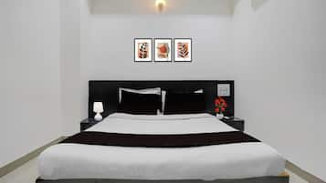Cama bem arrumada com esquema de cores preto e branco, mesa de cabeceira com luminária e três quadros na parede.