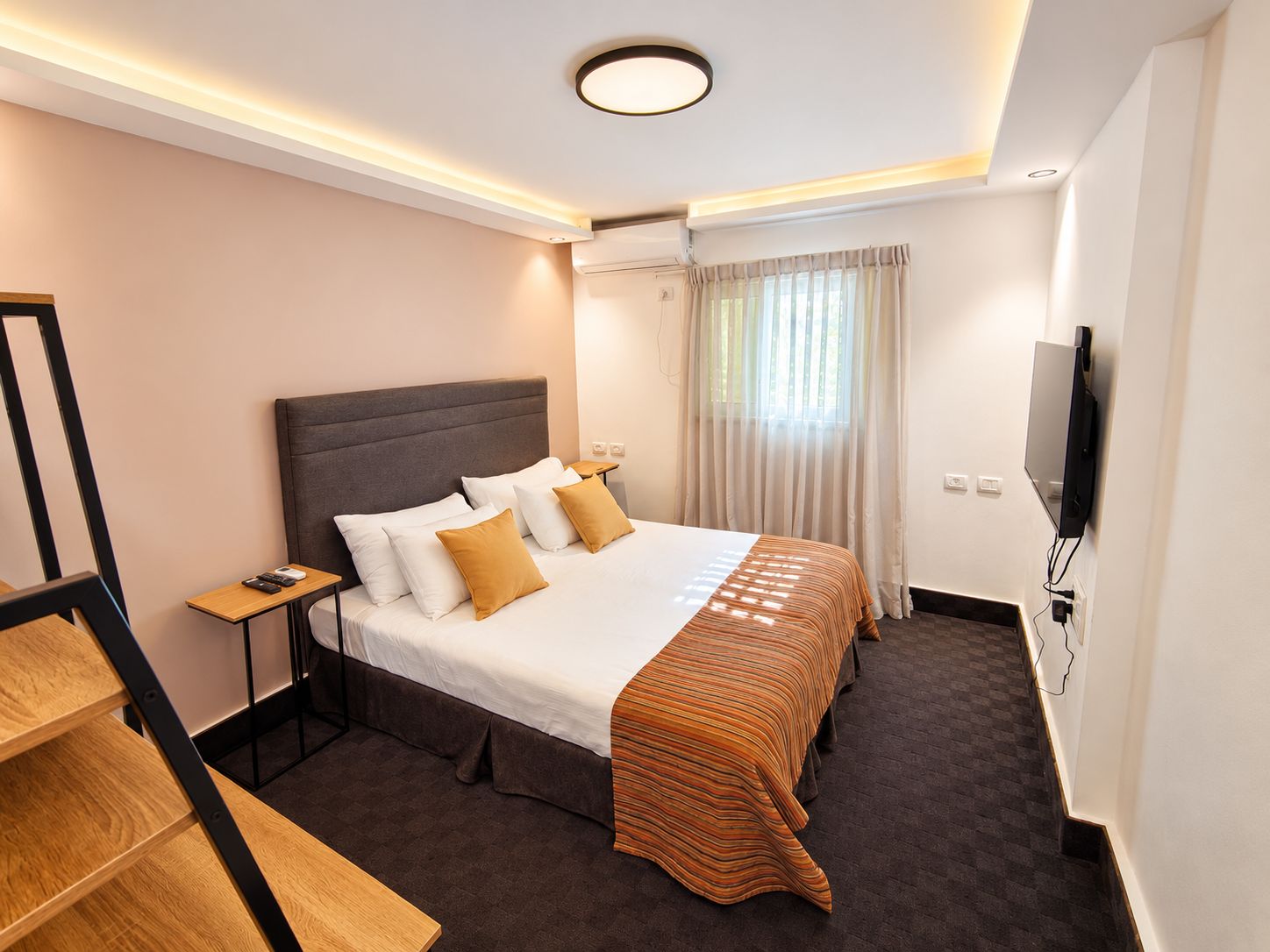 Quarto de hotel com cama, televisão, escrivaninha e janela com cortinas.