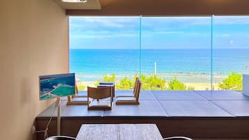 Quarto moderno com uma grande janela com vista para uma praia, uma mesa de madeira e duas cadeiras.