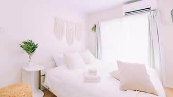 Quarto de hotel com cama, mesinha redonda, planta em vaso e janela com cortinas.