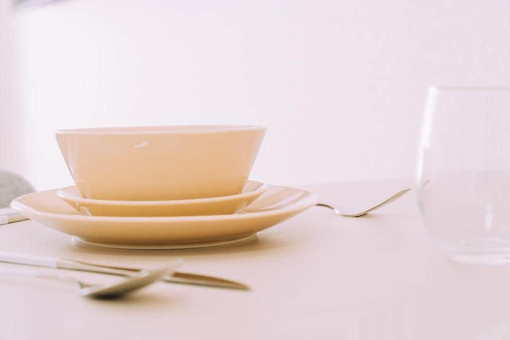 Uma mesa com uma pilha de pratos bege e um copo de vidro transparente.