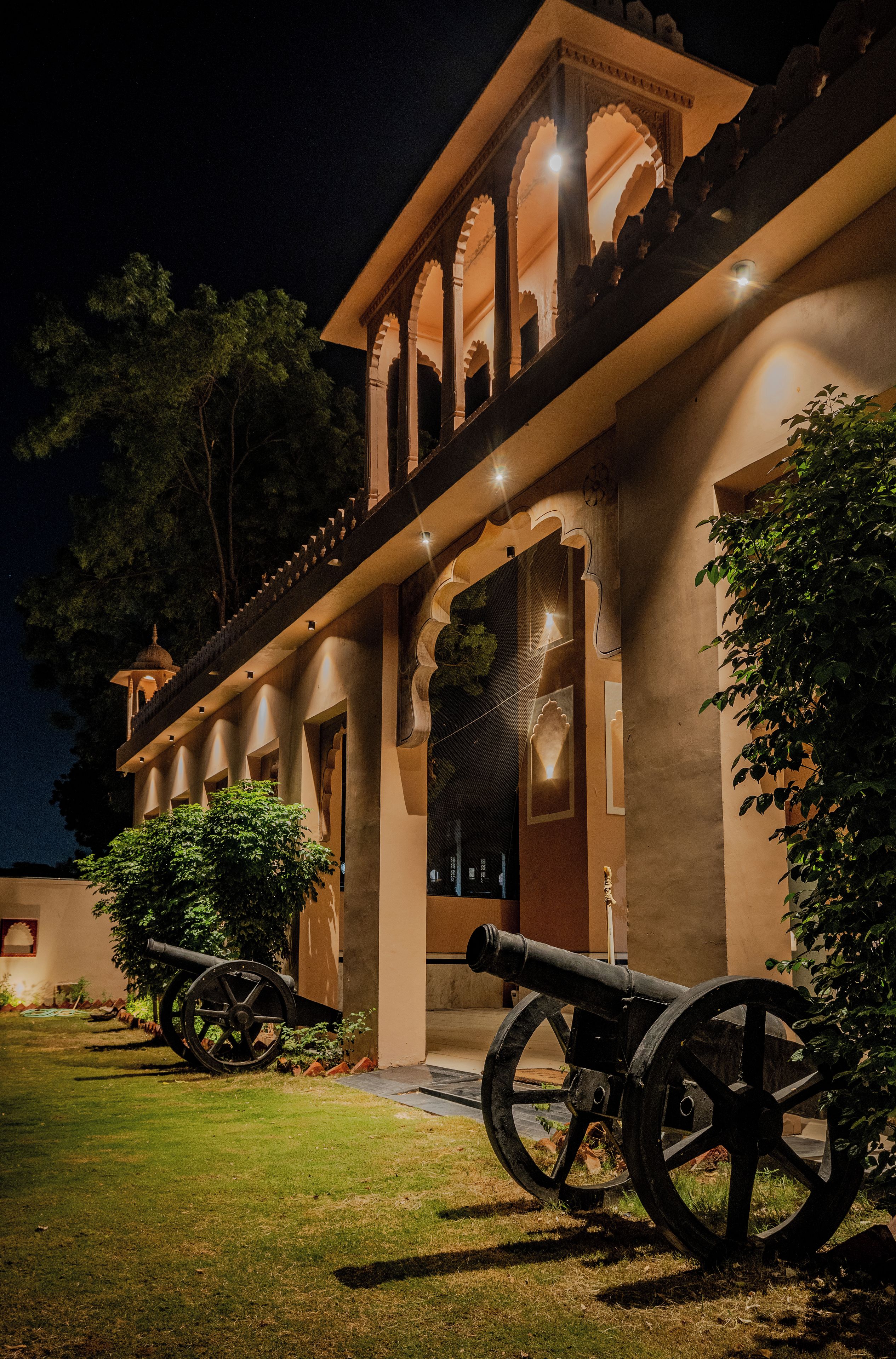 Um edifício com arquitetura tradicional, com arcadas e uma varanda. Dois canhões estão posicionados em primeiro plano.