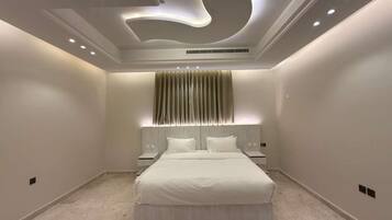 Quarto moderno com cama grande, iluminação embutida no teto e painel decorativo na parede.
