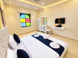 Quarto de hotel com cama, televisão, escrivaninha e armário com fotografias.