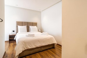 Quarto com cama, mesas de cabeceira e piso de madeira.
