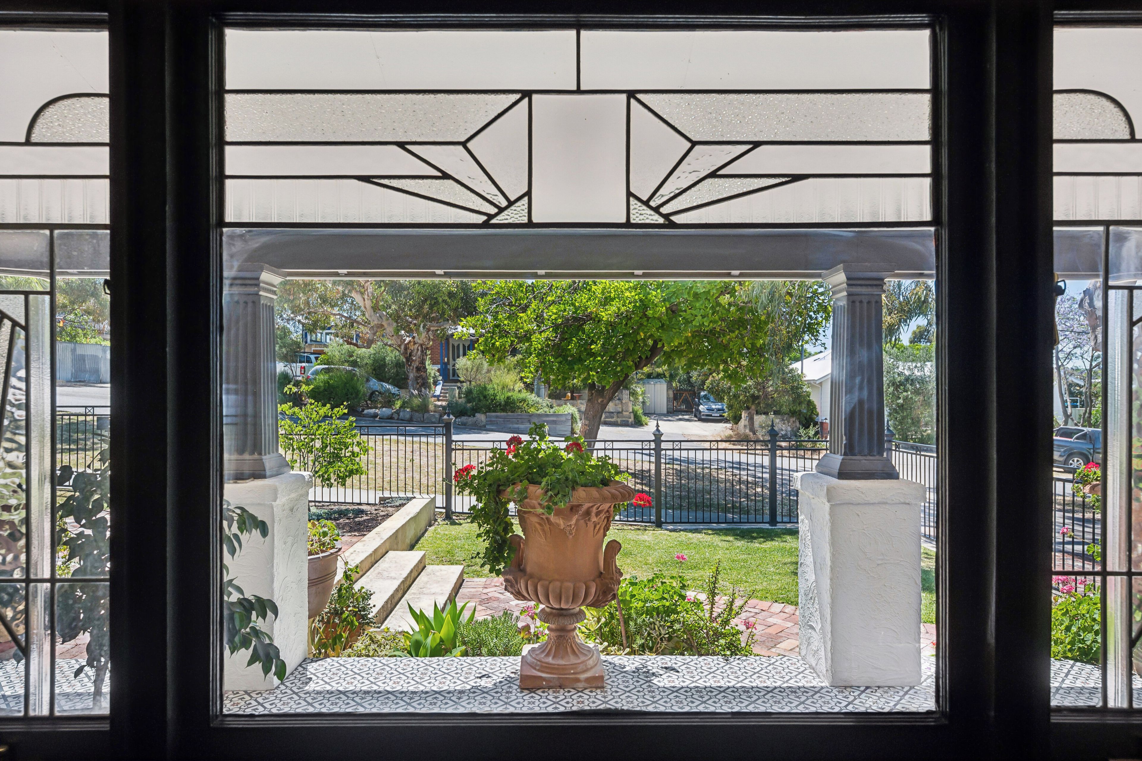 Vista pela janela com moldura decorativa, um vaso de planta e um espaço de pátio com azulejos.