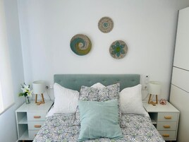 Quarto com cama, duas mesas de cabeceira e detalhes decorativos nas paredes.