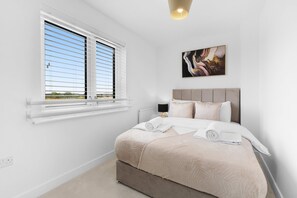 Quarto com cama, janela com persianas, radiador, quadro na parede e abajur.