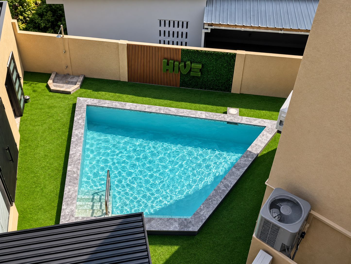 Piscina retangular com superfície de água azul cristalina, rodeada por grama sintética e cerca de madeira com logo verde.