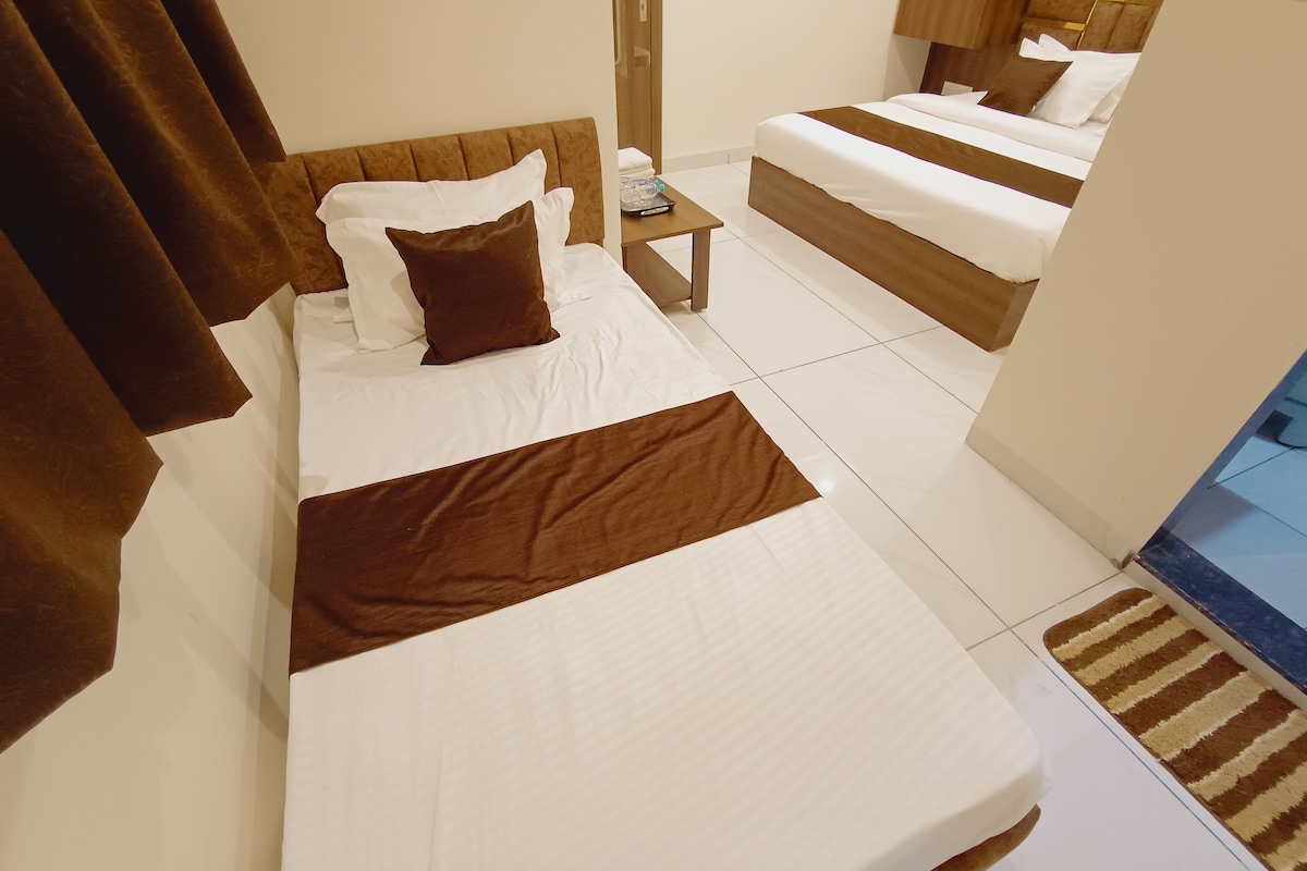 Quarto de hotel com duas camas, uma mesa de cabeceira e um banheiro visível no reflexo.
