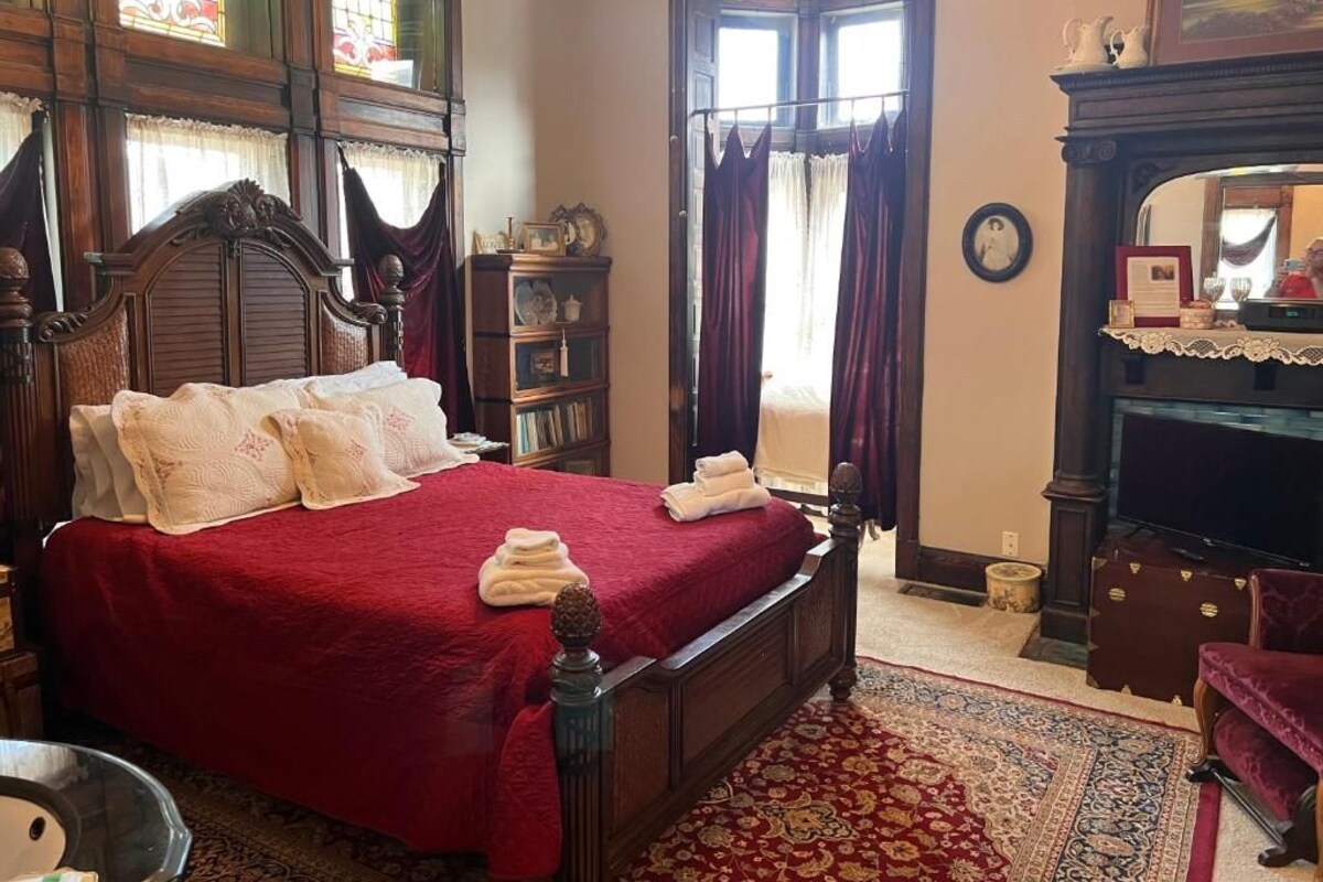 Quarto com uma cama grande, cômoda de madeira, televisão e lareira.