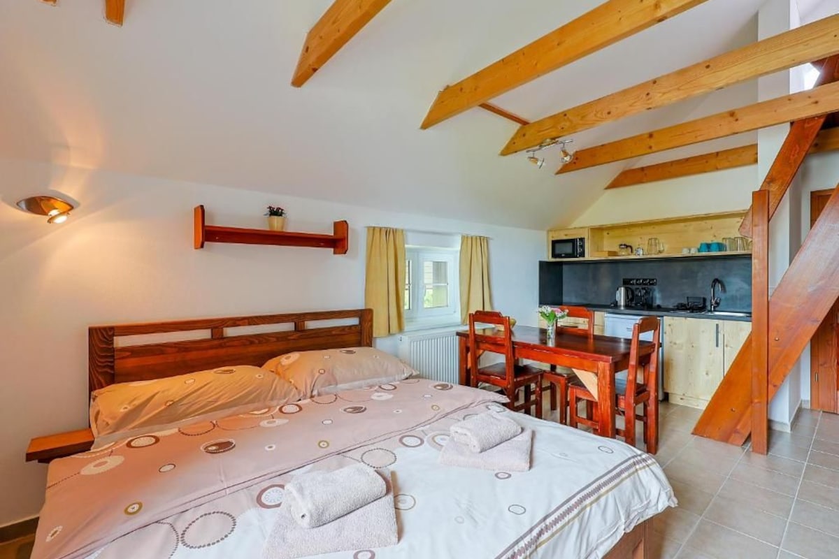 Quarto com cabeceira de madeira, cama com colcha estampada, mesa de cabeceira e pequena área de cozinha equipada com micro-ondas e chaleira.