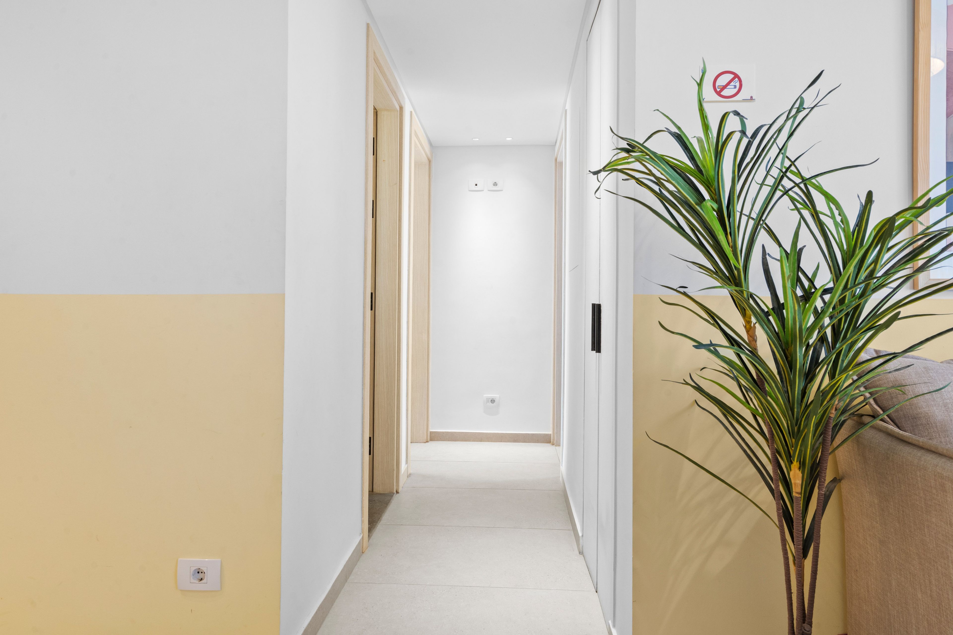 Corredor com uma planta, placa de proibido fumar e uma porta no final.