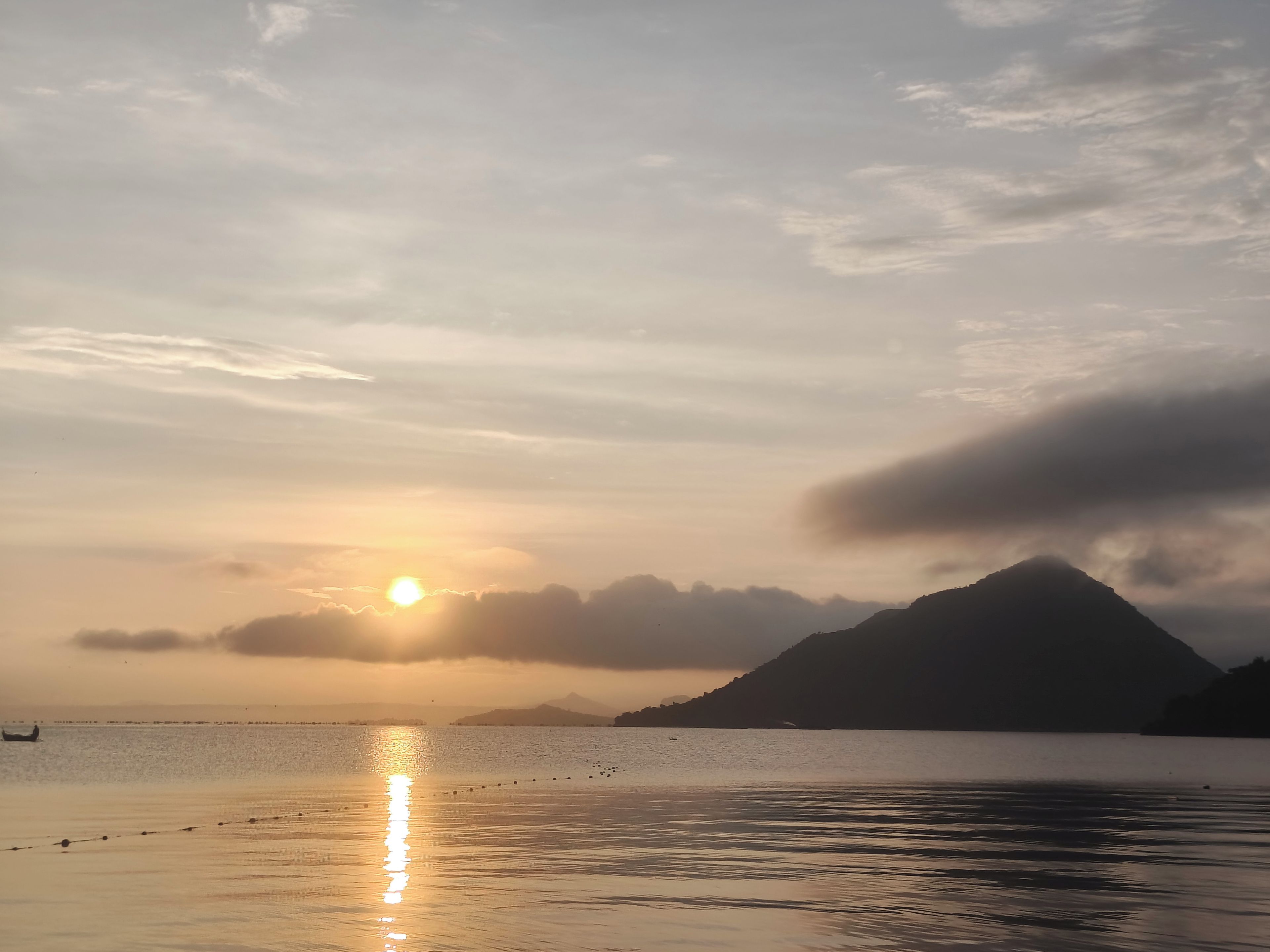 Um pôr do sol sobre águas calmas, com uma montanha ao fundo.