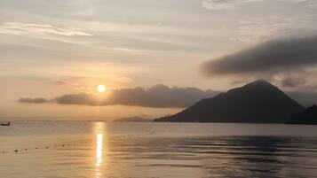 Um pôr do sol sobre águas calmas, com uma montanha ao fundo.