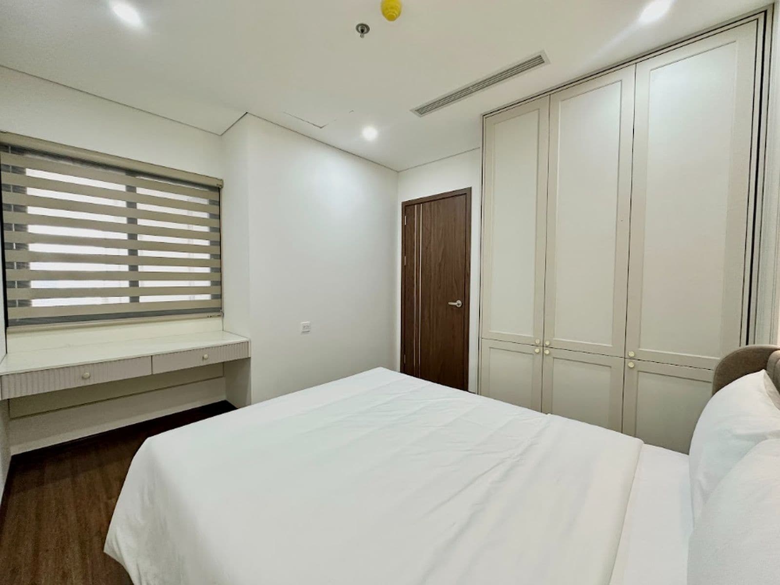Quarto com cama, janela com persianas, guarda-roupa e mesa de cabeceira.