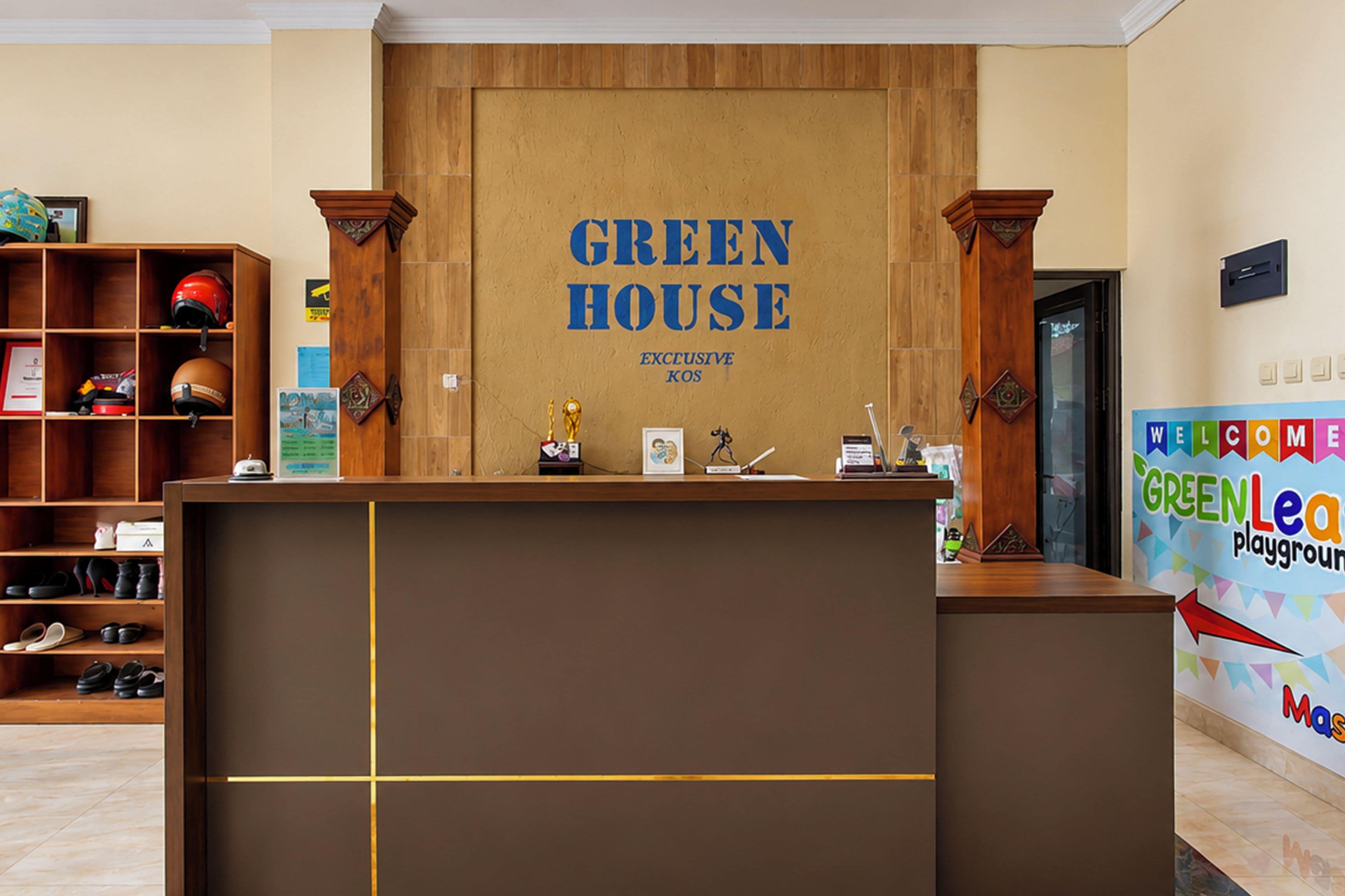 Balcão de recepção com a placa 'GREEN HOUSE', um troféu e um letreiro de 'BEM-VINDO' com letras coloridas.