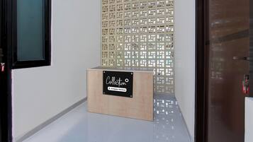 Uma área de recepção com balcão de madeira identificado como 'Collection' e um painel decorativo com padrão geométrico.