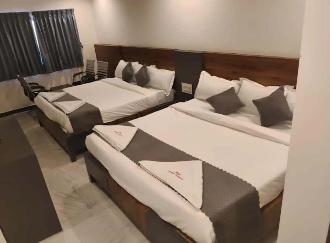 Quarto de hotel com duas camas, cabeceira de madeira e janela com cortinas.