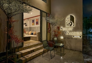 Exterior do Hotel Secret Garden, com placa, degraus para a entrada e área de estar ao ar livre.
