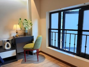 Quarto com escrivaninha, cadeira, luminária e uma grande janela com vista.