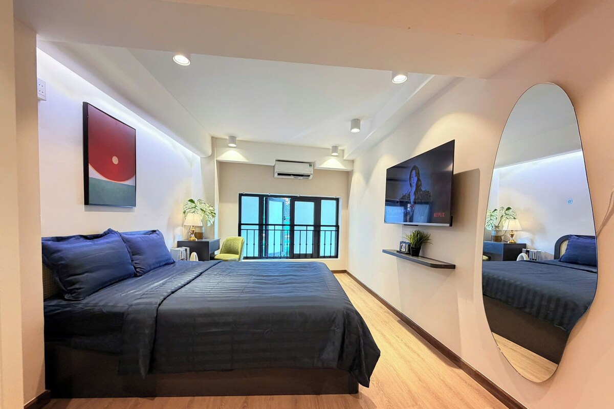 Quarto de hotel moderno com cama grande, televisão de tela plana, varanda com vista e um espelho amplo.
