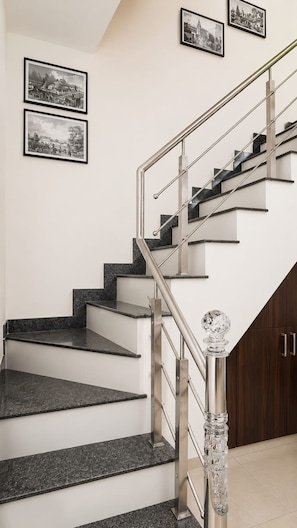 Uma escadaria com balaustrada de vidro, ornamento de cristal e três fotografias a preto e branco emolduradas na parede.