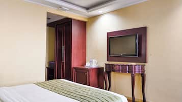 Quarto de hotel com uma cama, televisão fixada na parede, um armário de madeira e uma porta que dá para outro cômodo.
