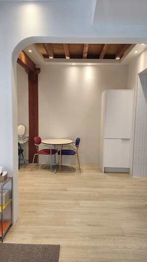 Quarto com teto de madeira, parede branca, armário branco e mesa redonda com cadeiras.