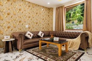 Quarto com sofá de couro marrom, mesa de centro de vidro, tapete estampado e janela com cortinas.